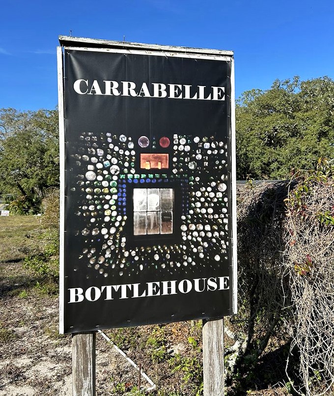 The Carrabelle Bottle House sign proudly displays the distinctive bottle pattern that has made this roadside attraction a must-see along Florida's Forgotten Coast.