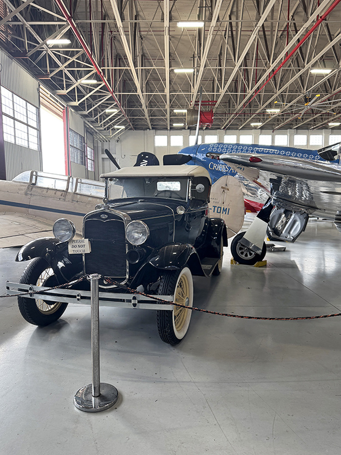 This vintage Ford Model A sits beneath aircraft wings, showing how Americans transitioned between ground and air transportation during the early 20th century.