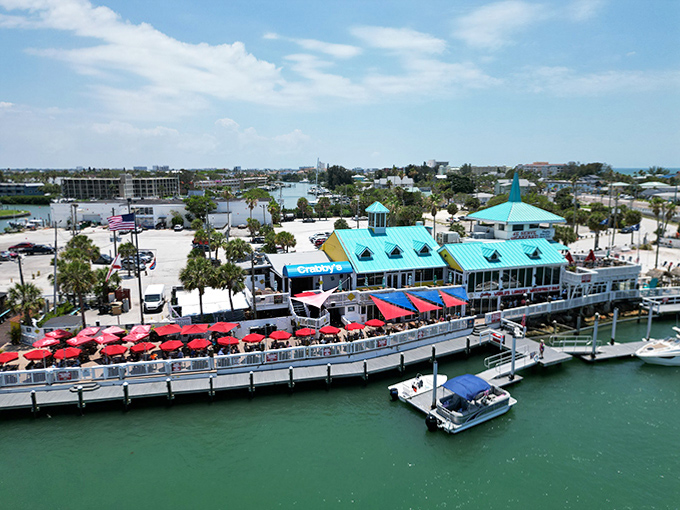 Aerial view of waterfront dining where red umbrellas pop against turquoise waters – seafood tastes better with this view.