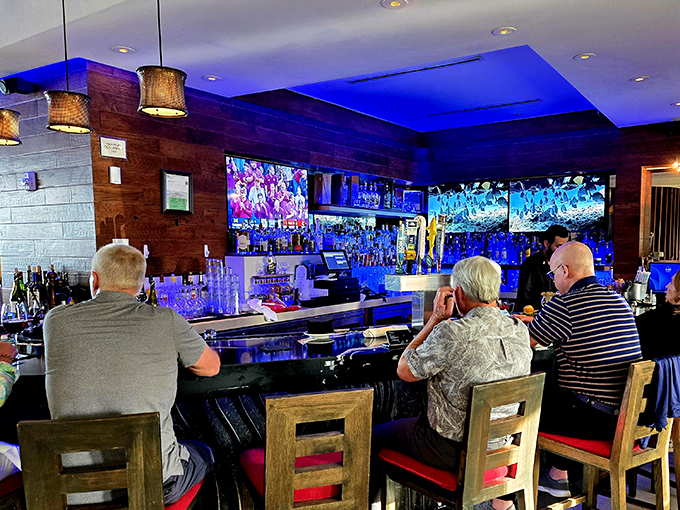 The bar glows with blue light as patrons perch on wooden stools, screens flickering above bottles that promise libations to complement any meal.