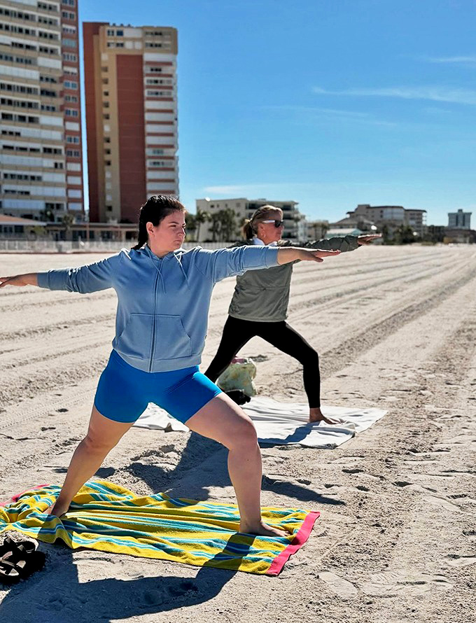 Two practitioners in warrior pose reach toward the horizon, their blue workout clothes matching the perfect Florida sky as they strengthen both body and spirit.