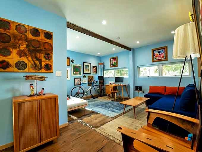 Upstairs, blue walls create a serene backdrop for eclectic art pieces, while wooden floors add warmth to the container's industrial bones.