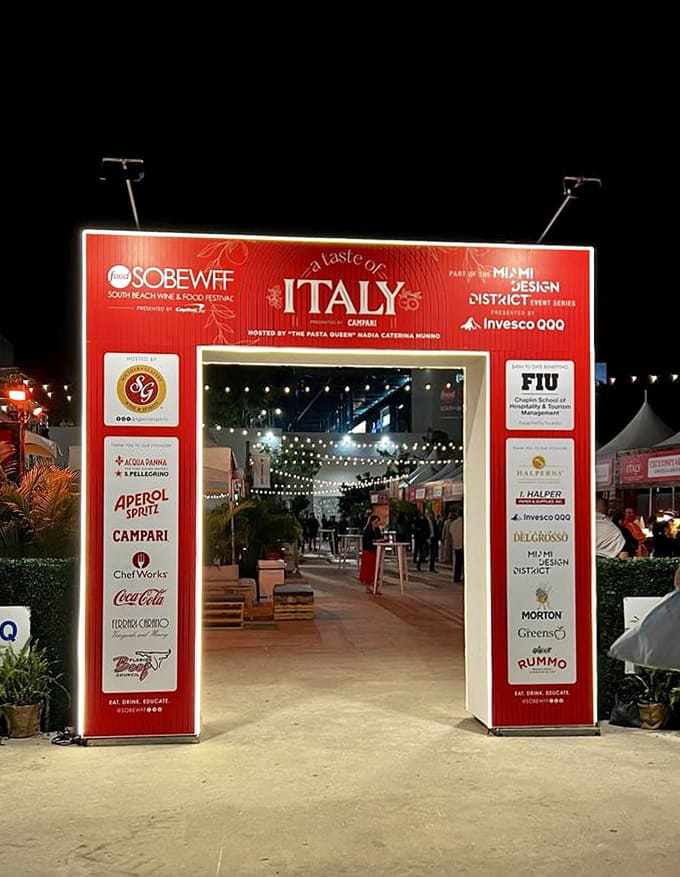 Night falls on the festival grounds as glowing signs guide food lovers toward their next delicious discovery in this culinary wonderland.