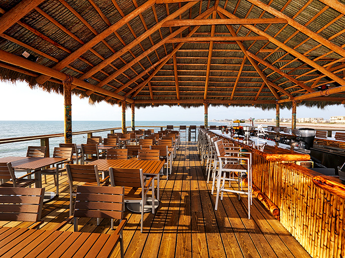 Empty morning tables await the day's guests, wooden surfaces gleaming under the thatched roof with endless ocean views beckoning beyond.