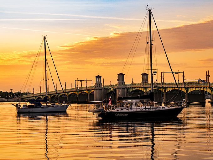 Sunset turns the water into liquid gold while boats drift beneath the bridge, creating a scene worthy of a tourism brochure.