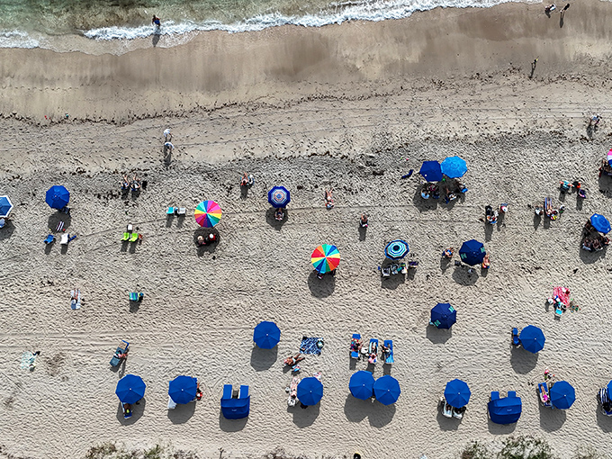 Beach umbrellas create a colorful mosaic against golden sands &ndash; each one sheltering stories, snacks, and sunbathers taking a break.