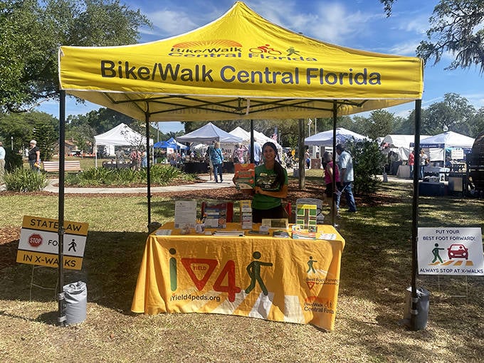 Festival-goers gather at the Bike/Walk Central Florida booth. This sunny spot offers information about pedestrian safety while celebrating community connection.