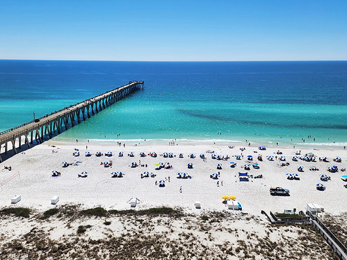 Beachgoers create a colorful mosaic below, tiny specks of joy against the white canvas of sand.