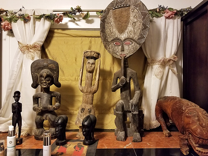 African tribal art creates a striking display against golden fabric, showcasing the eclectic collection of artifacts that give each room its unique character.
