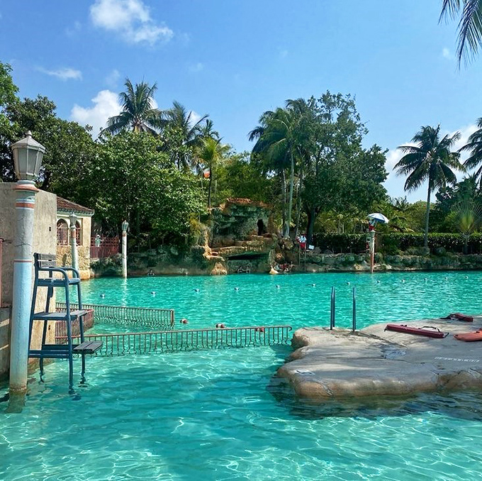The lifeguard station stands ready beside mysterious cave openings, where swimmers can explore cool grottos carved from natural coral formations.