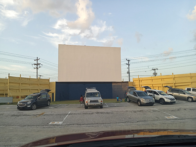 Early arrivals claim prime viewing spots, creating a patchwork of vehicles all facing the blank canvas that will soon flicker to life.