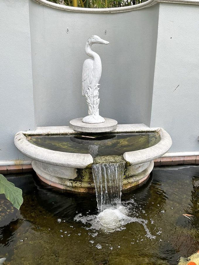 A white heron stands frozen in artistic perfection, water cascading around its elegant form in this charming fountain vignette.