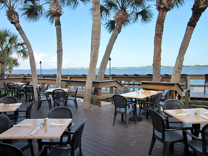 Palm trees frame waterfront tables where diners enjoy meals with unobstructed views of the Indian River Lagoon stretching to the horizon.