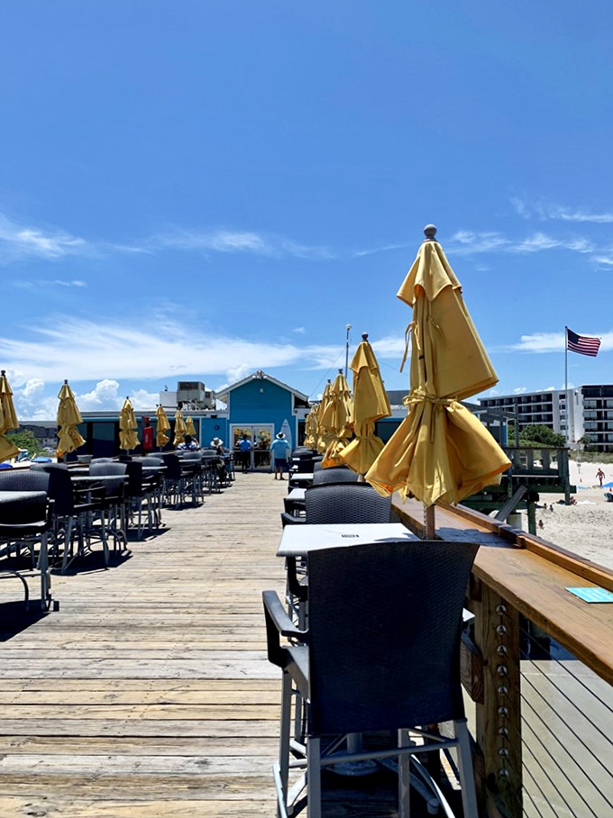 Yellow umbrellas stand at attention along the wooden pier, offering shade for those who prefer their ocean views without the full Florida sunshine.