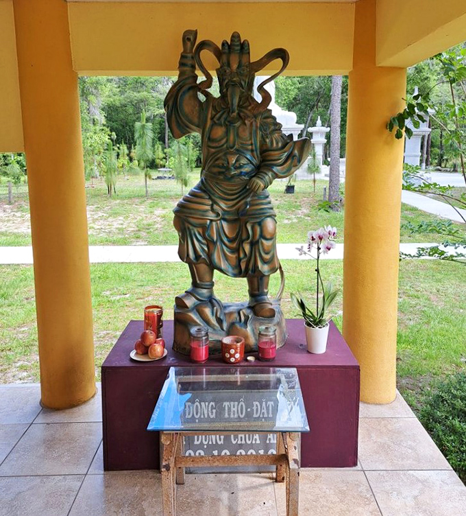 A guardian deity stands watch with dramatic expression and powerful stance, offering striking contrast to the serene Buddha figures nearby.