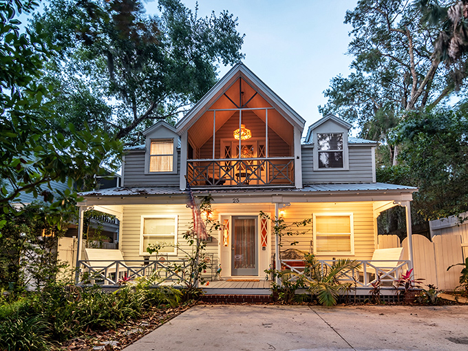 This two-story porch house glows with warm welcome at dusk, its lights beckoning beneath the ancient oaks' protective embrace.