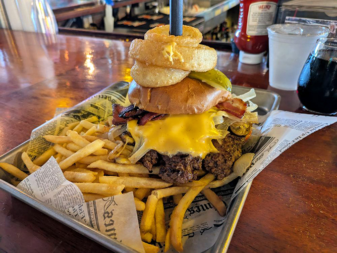 A towering monument to excess, where onion rings crown a juicy patty in a delicious challenge that requires both hands and total commitment.