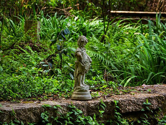Silent storyteller: Garden statuary stands watch among the ferns, weathered by seasons yet still maintaining its quiet dignity.