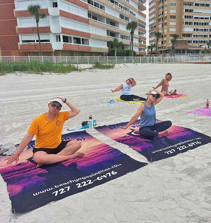 A happy group strikes playful poses on their beach yoga mat, the ocean stretching endlessly behind them like nature's own version of a deep breath.