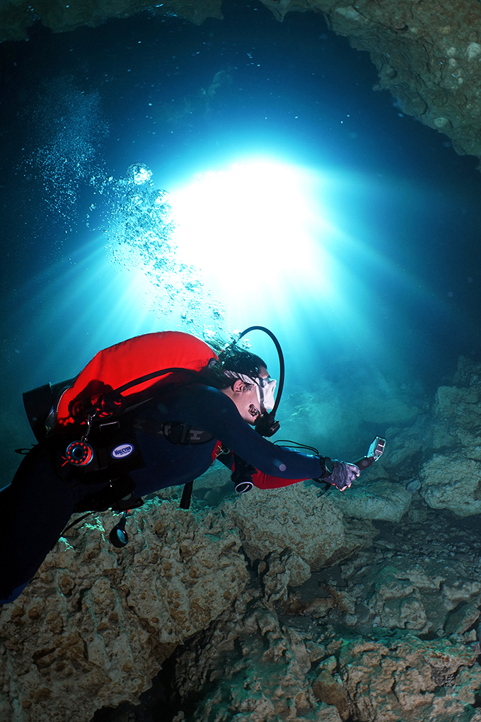 A diver explores underwater passages where sunlight creates ethereal blue spotlights, turning limestone caves into nature's most exclusive theater.