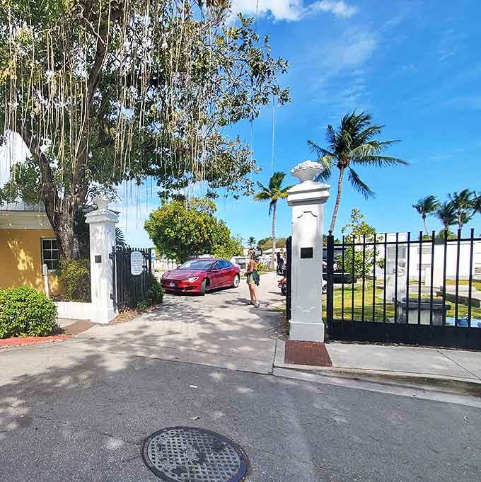 The cemetery's wrought iron gate stands open between white pillars, welcoming both the curious tourist and the reverent mourner.