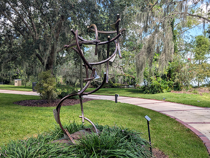Curved metal sculpture rises from manicured grounds, its abstract form creating different silhouettes as visitors circle it on the winding garden path.