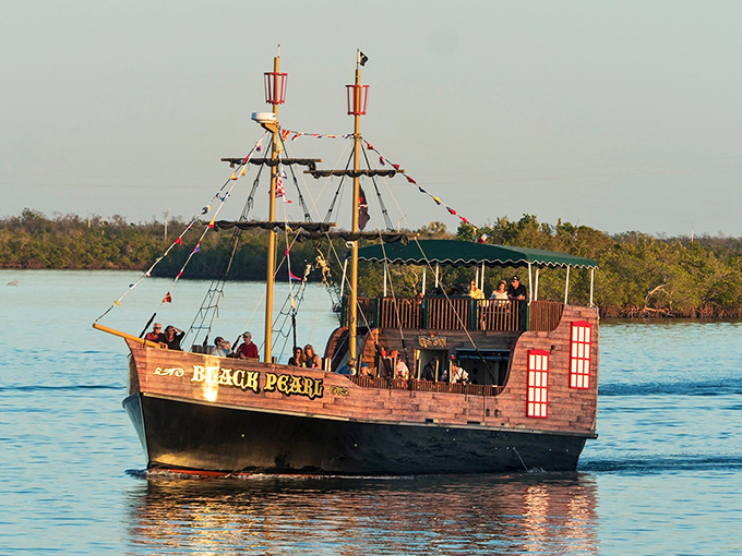 The Black Pearl glides through Marco Island's waters at sunset, its wooden hull gleaming like buried treasure in the golden light.