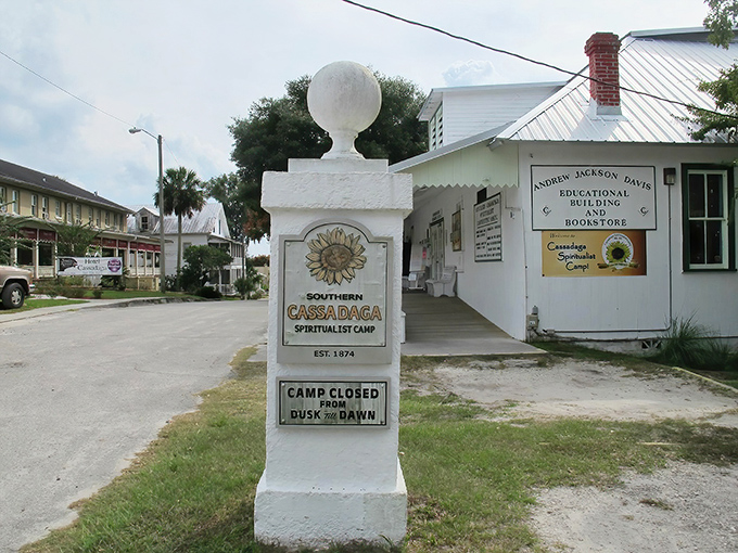 The entrance to Southern Cassadaga Spiritualist Camp welcomes visitors with its distinctive white pillars and sunflower emblem, a beacon for spiritual seekers since 1894.