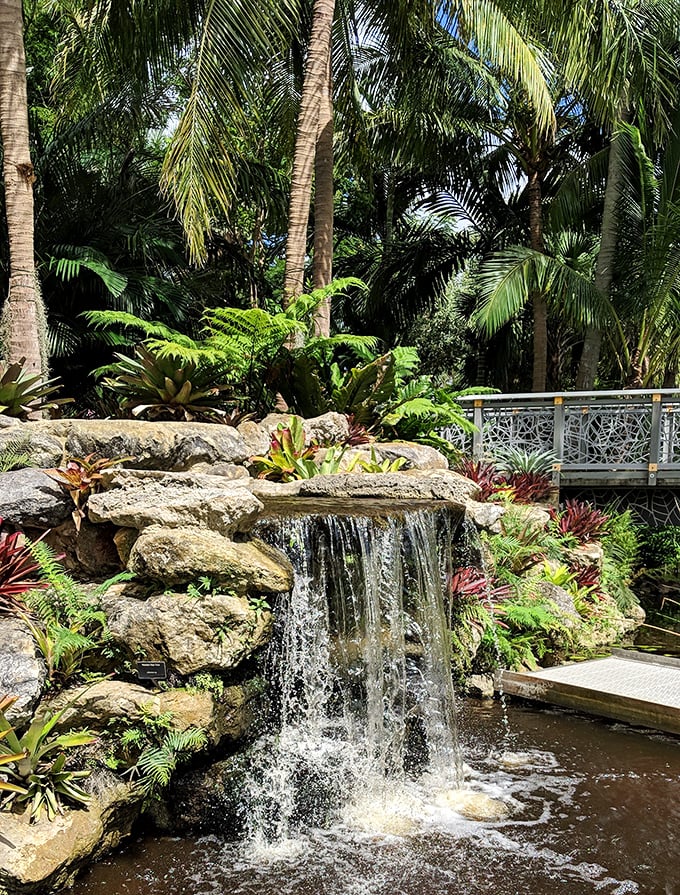 Water cascades over natural stone, creating nature's soundtrack in this tranquil corner where tropical plants thrive in the mist.