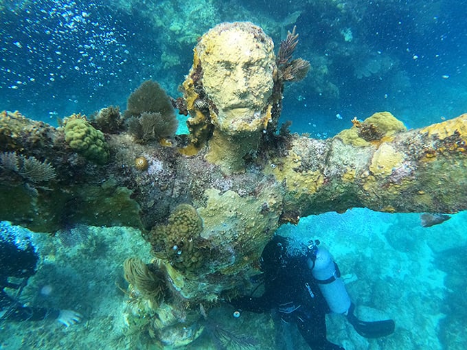 Encrusted with colorful marine growth, the statue's face gazes eternally upward, a silent witness to the ever-changing underwater world around it.