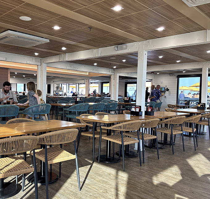 The interior blends casual beach vibes with practical comfort – wooden tables, rope-backed chairs, and panoramic ocean views from every seat.