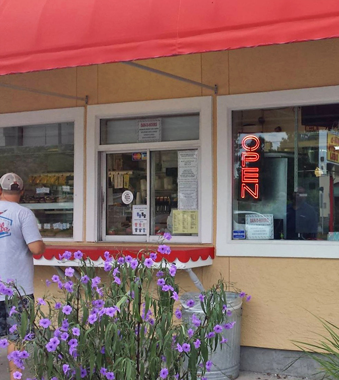 The walk-up window, framed by purple flowers, offers a glimpse into a world where donuts aren't just breakfast &ndash; they're an art form.