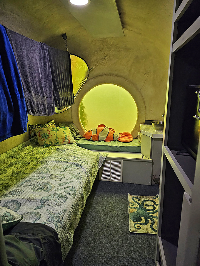 The cozy underwater bedroom features ocean-themed decor and a circular window offering mesmerizing views of marine life swimming by.