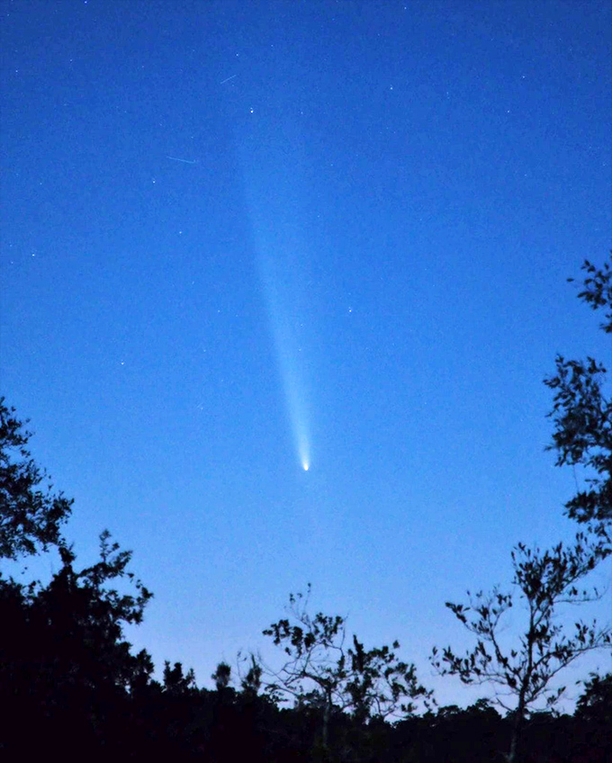 A celestial visitor streaks across the twilight sky, its glowing tail a cosmic exclamation point against the deepening blue.