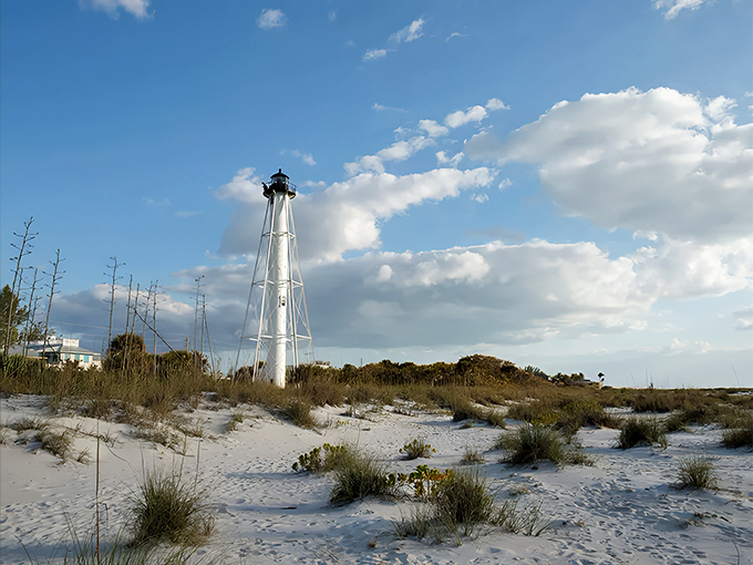 The historic lighthouse stands sentinel over Boca Grande's shoreline, where sea oats dance in the breeze against a backdrop of endless blue sky.