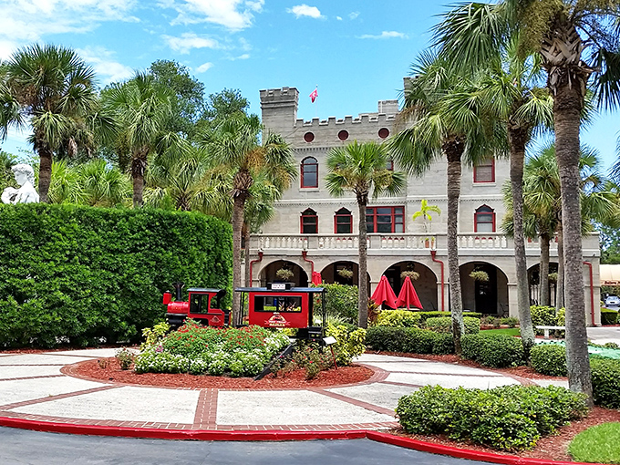 The charming entrance to Warden Castle welcomes visitors with bright red accents, lush gardens, and a miniature train &ndash; a whimsical gateway to oddities within.