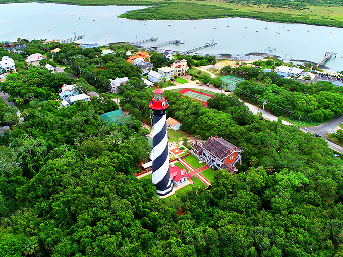Aerial view: From above, the lighthouse stands like a chess piece on a lush green board, surrounded by the blue waters that have claimed countless ships.
