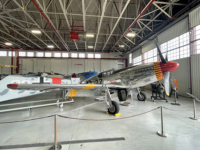 A silver P-51 Mustang gleams under spotlights, its sleek aluminum body and distinctive red-tailed paint scheme honoring the legendary Tuskegee Airmen who flew similar aircraft.