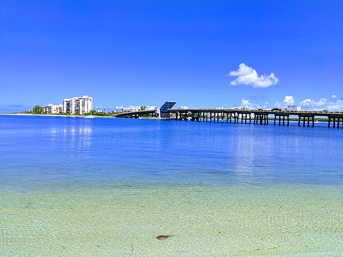 The sun-drenched causeway connecting mainland dreams to island reality, with azure waters stretching toward the horizon.