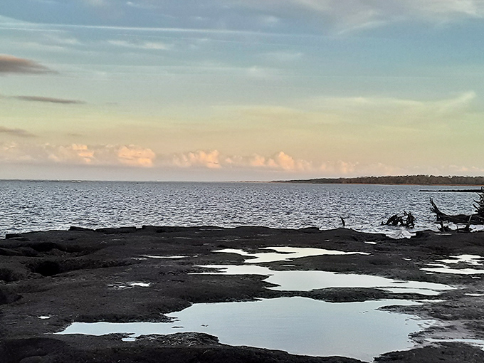 Twilight transforms the coastline into a moody canvas, with gentle waves lapping against the shore as clouds gather on the horizon.