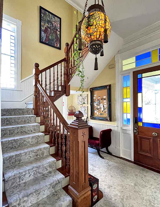 The grand staircase welcomes you with warm wood tones and a hanging Tiffany-style lamp that casts a honeyed glow over the entryway's vintage charm.