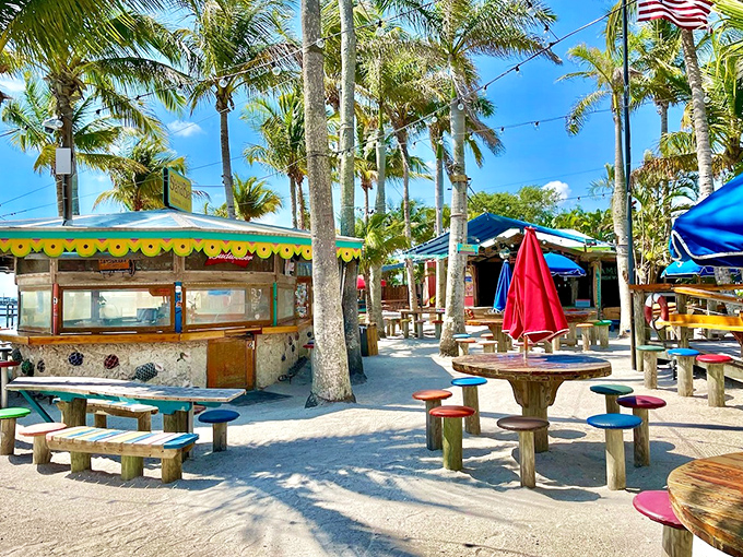 Captain Hirams brings beach party vibes with colorful picnic tables nestled in real sand under swaying palm trees.