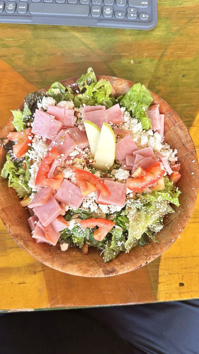 Fresh salad served in a wooden bowl brings balance to pizza indulgence. Ham, tomatoes, and feta create a colorful counterpoint.