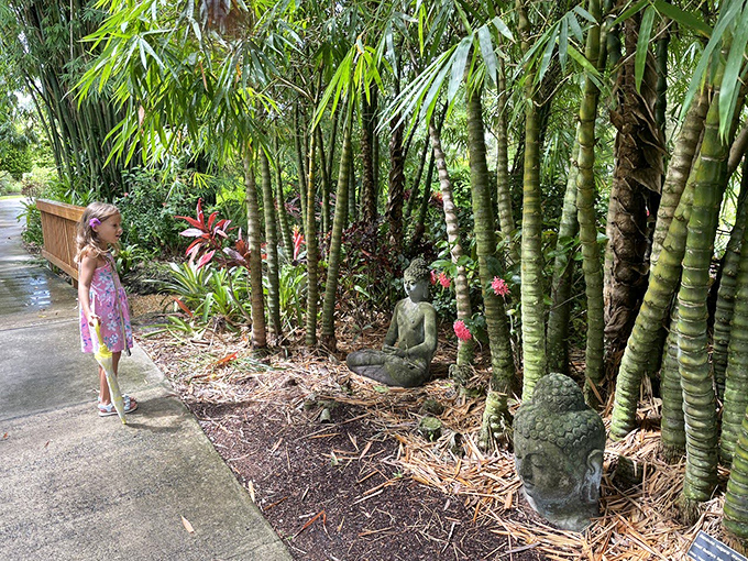 Bamboo sentinels stand guard along the pathway where stone Buddhas meditate among tropical foliage, offering moments of zen.