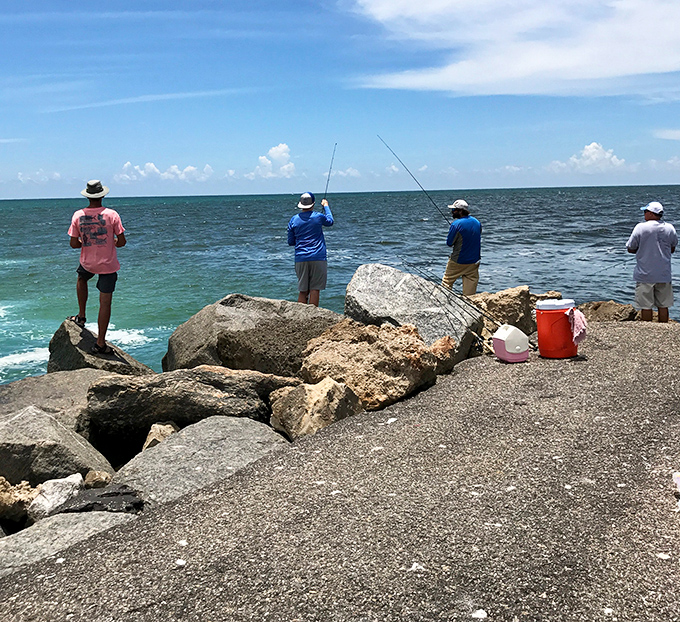 Anglers perch on jetty rocks like patient herons, their fishing lines dancing in Gulf waters teeming with snook and redfish.