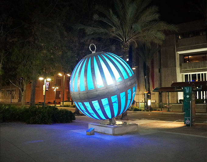 When darkness falls, the sculpture transforms into a glowing blue beacon, its illuminated panels creating an otherworldly atmosphere that captivates evening strollers.