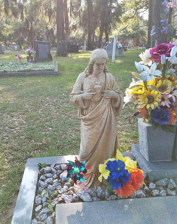 This weathered statue watches over its plot with quiet dignity, fresh flowers suggesting someone still remembers the story behind the stone.