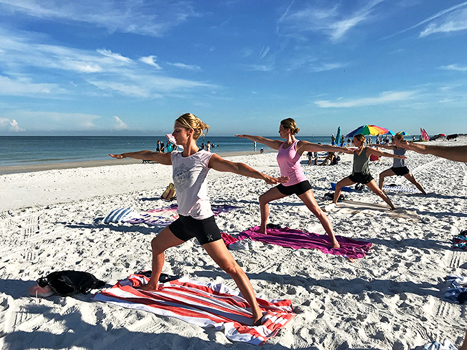 Four women in warrior poses face the ocean, their colorful mats creating a vibrant contrast against the white sand while Florida's famous sunshine beams down approvingly.