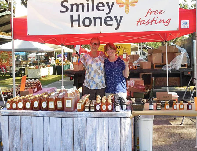 Smiley Honey vendors beam with pride behind their table of golden jars, ready to share nature's sweetest treasure with festival visitors.