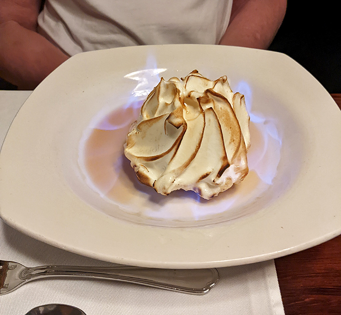 The Baked Alaska arrives like a meringue-capped mountain, torched tableside with enough dramatic flair to earn a standing ovation.